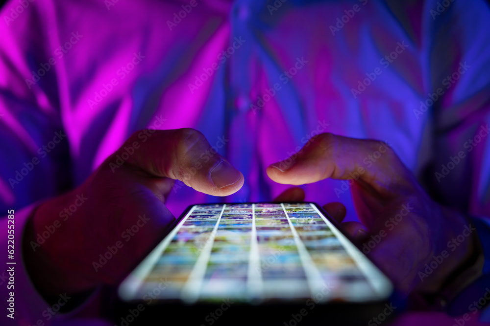 man scrolling mobile phone screen in dark room with neon lights. internet browsing, social media ...