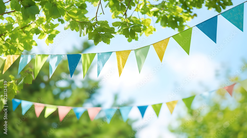 colorful pennant string decoration in green tree foliage on blue sky ...