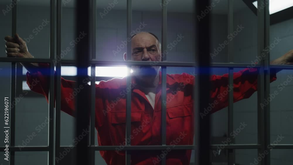 Elderly prisoner in orange uniform holds hands on metal bars in jail ... Elderly prisoner in orange uniform holds hands on metal bars in jail ...