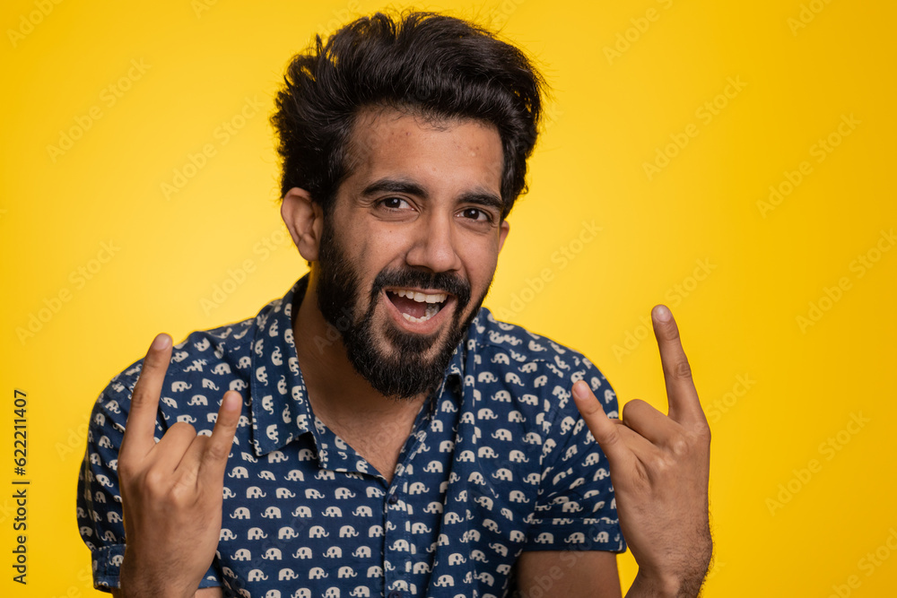 Overjoyed young indian man showing rock n roll gesture by hands, cool ...