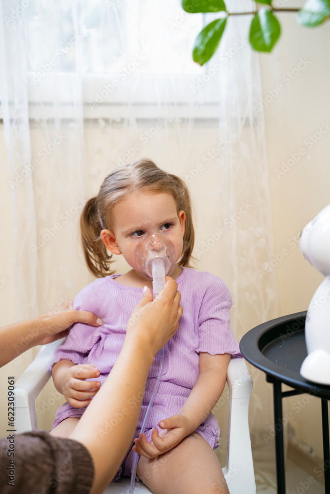 Cute little girl uses inhaler at home. Holding mask over her nose and ...
