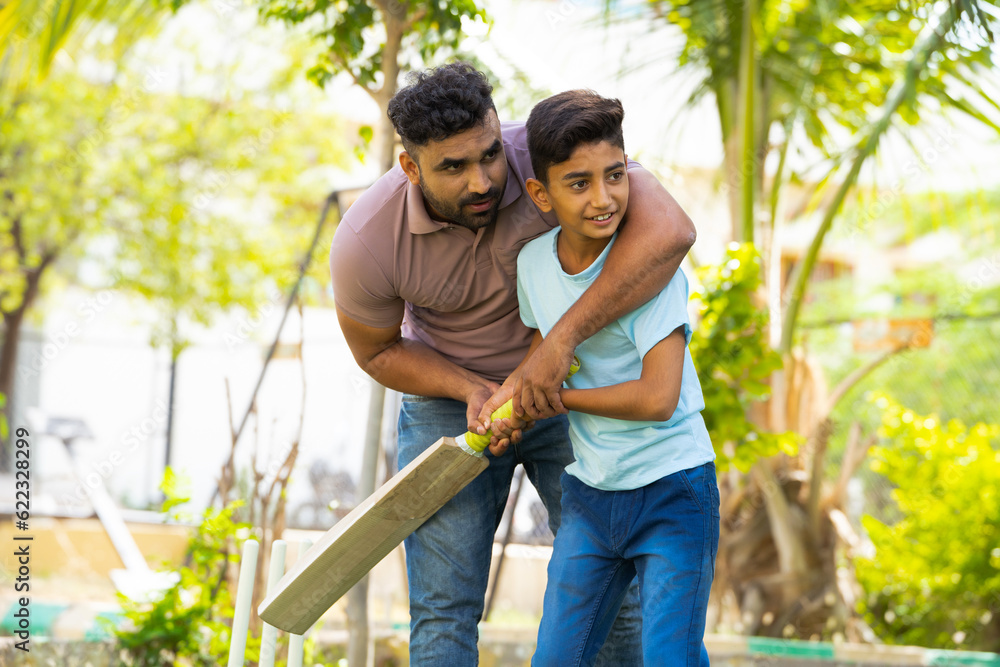 indian father teaching his son to playing cricket game at park ...