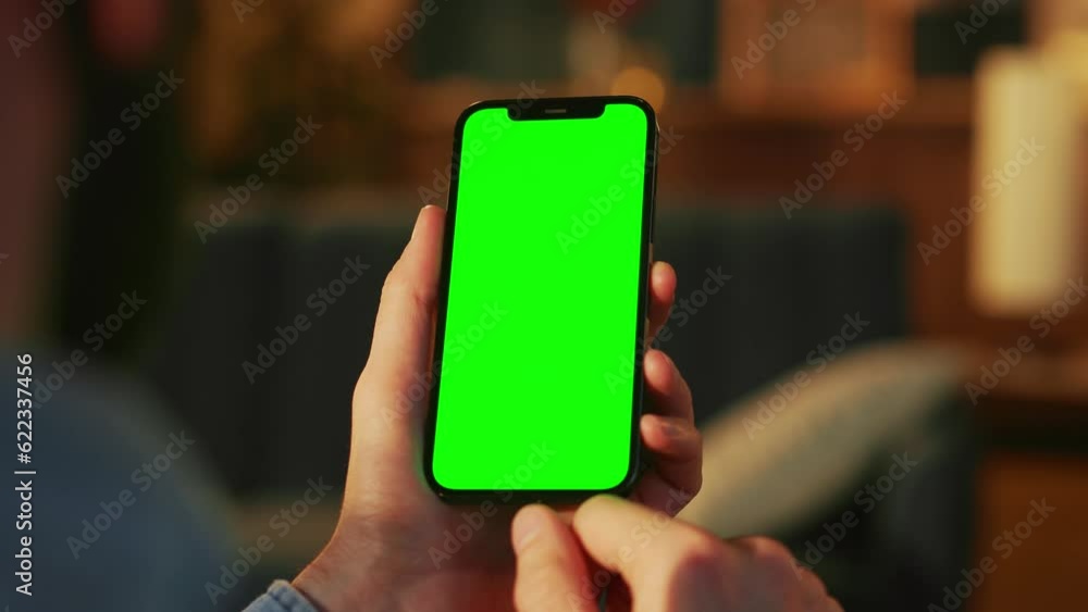 Man's hands holding smartphone with green screen on blurred background ...