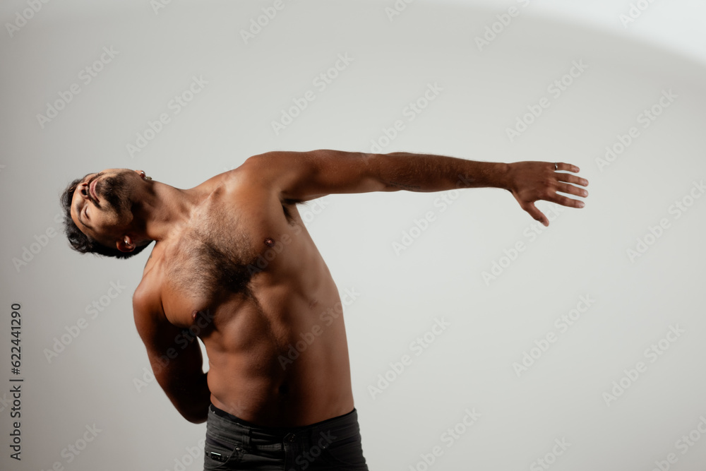 A shirtless man leans back, letting the light hit his muscular chest ...