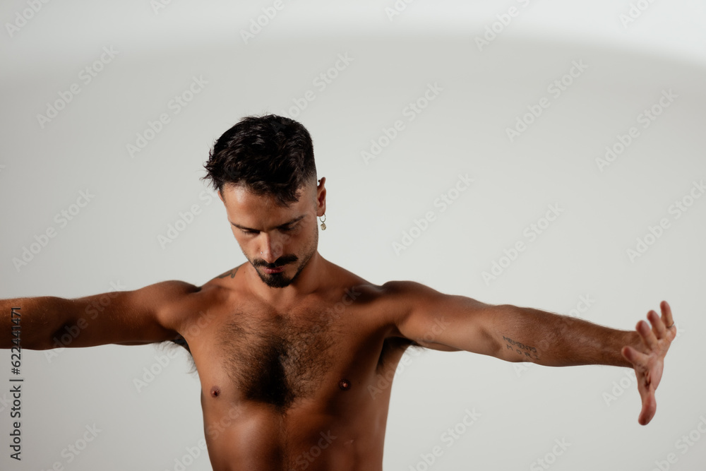 A shirtless man extends his arms outward, filling the frame and ...