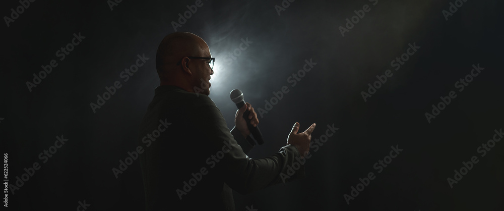 Confident successful speaker man talking on stage with spotlight strike ...