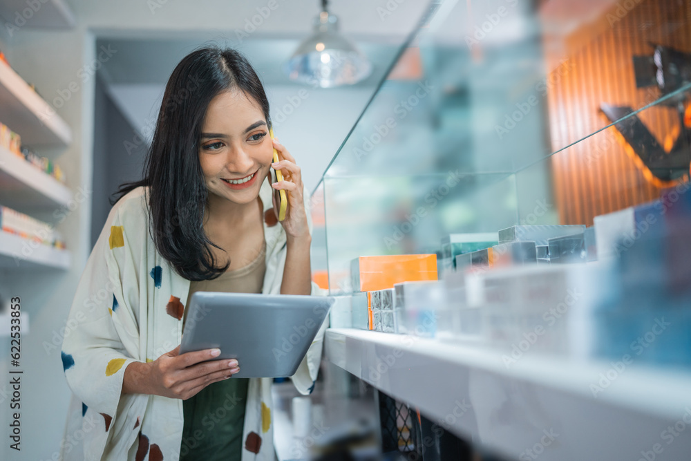 female shopkeeper calling on phone while checking the vape mods stock ...