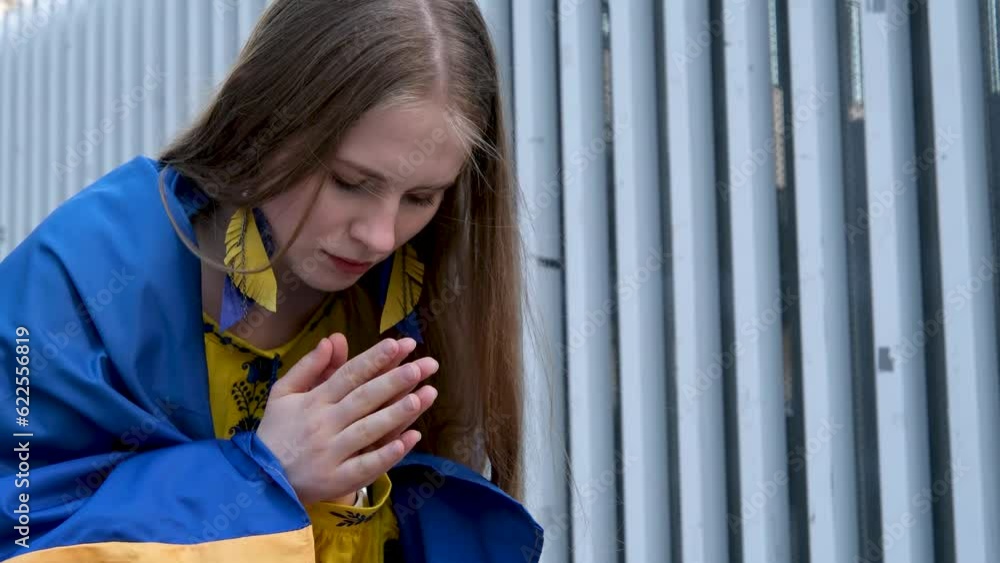 Ukrainian girl with Ukrainian flag on shoulders prays with hands folded ...