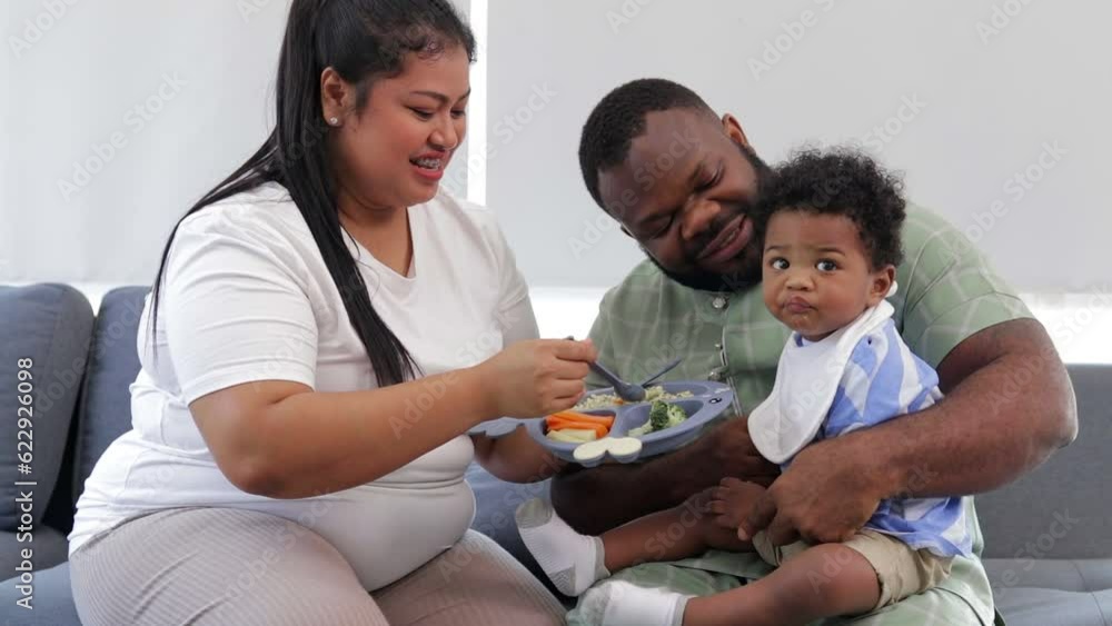 The boy smiled happily with his mother and father as they ate in the living room at home ...
