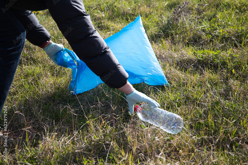 Hand detail of a volunteer collecting plastic bottle from the forest to ...