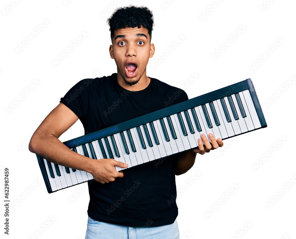 Young african american man holding piano keyboard afraid and shocked ...