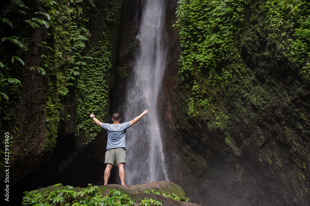 Back view of a man standing by waterfalls with arms outstretched. Man ...