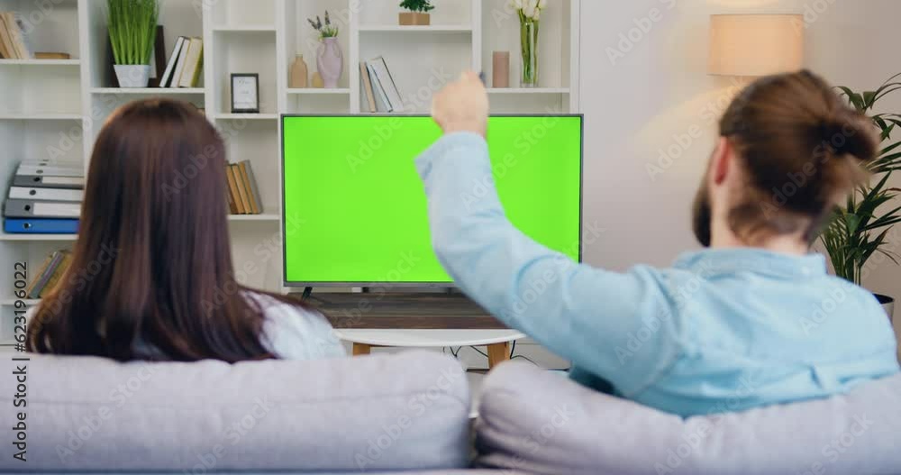 Happy couple watching tv and switching channels looking at green screen ...