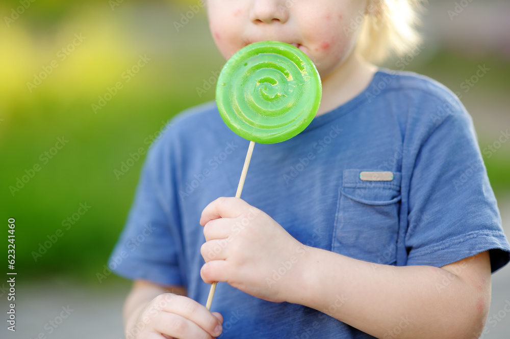 Child with allergic reaction eating big green lollipop. Unhealthy sweet ...