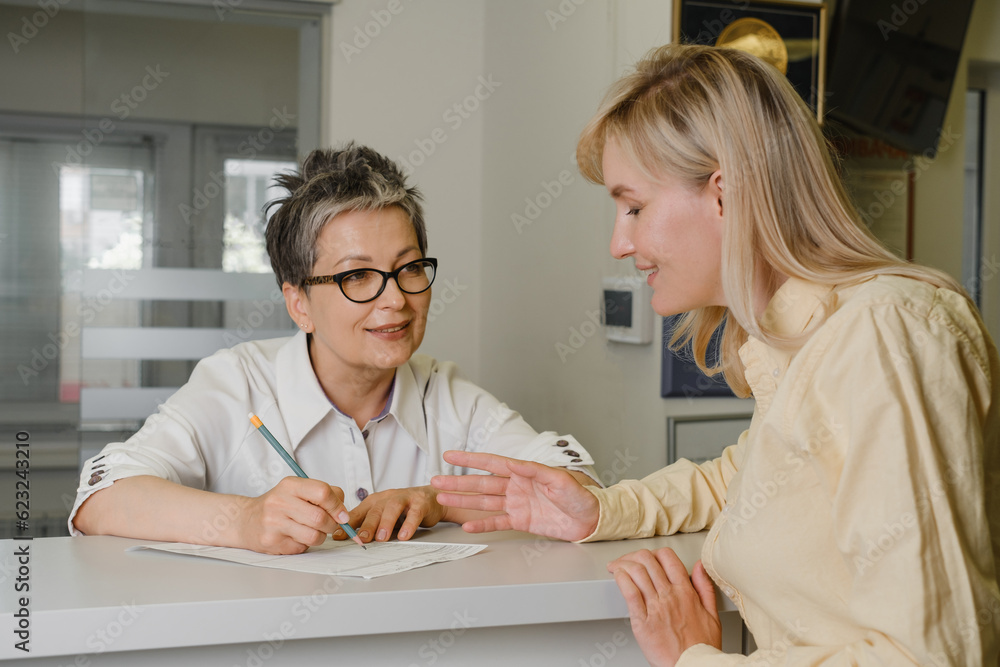 Patient at reception desk of clinic talking about her appointment ...