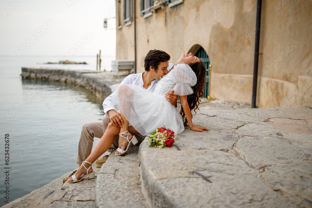 Stylish bride in short wedding dress and groom sitting at old Italian ...