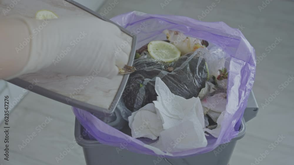 Person in rubber gloves throws food waste from wooden cutting board ...