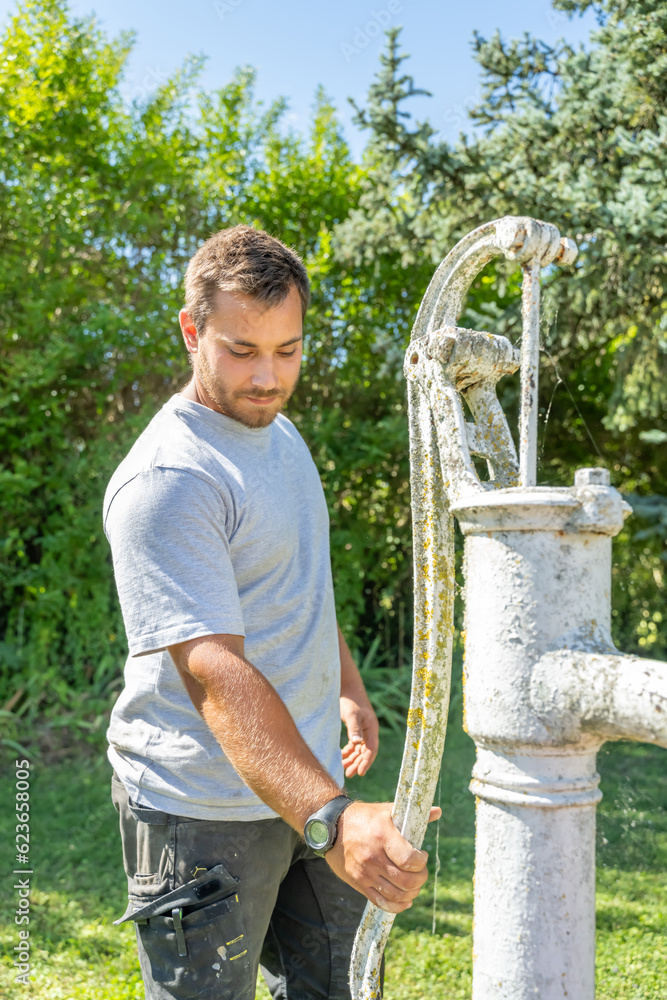 Jeune homme dans un jardin se servant d'une pompe à eau pour puiser de ...