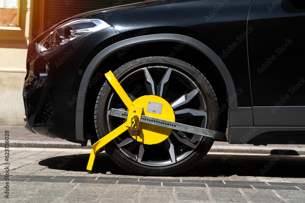 Car wheel blocked by a yellow metal lock or clamp. Vehicle illegal ...