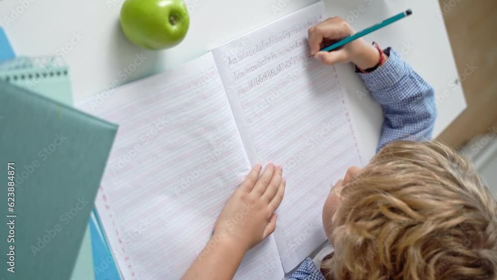 Elementary school student boy or girl writing letters, studying at desk ...