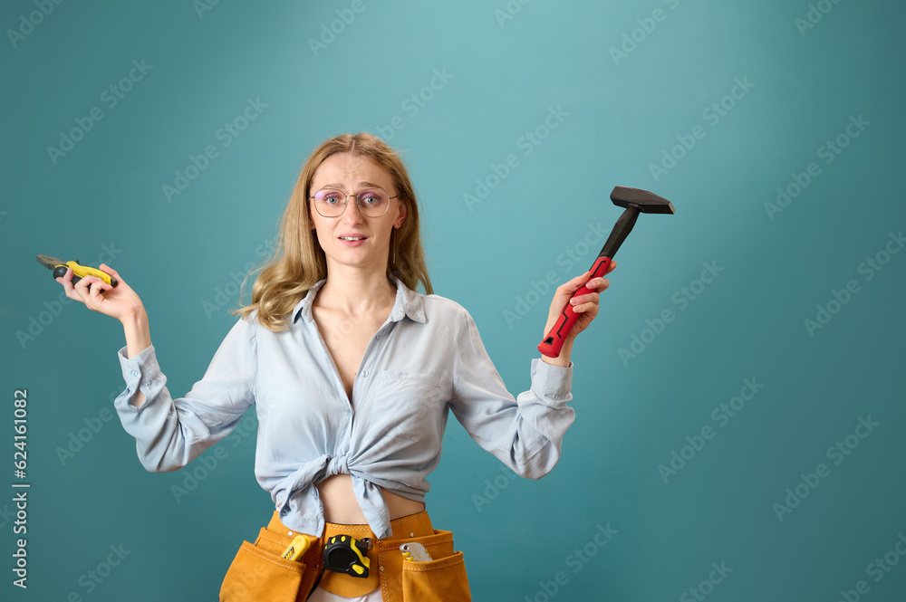 Portrait of surprised young female worker with tool belt holding a ...