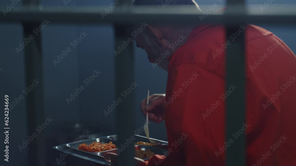 Close up of elderly prisoner in orange uniform sitting in prison cell ...