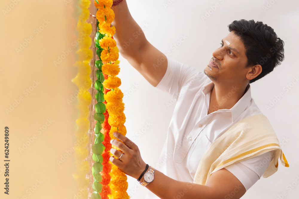 South Indian man decorating house with flower garland to celebrate Onam ...