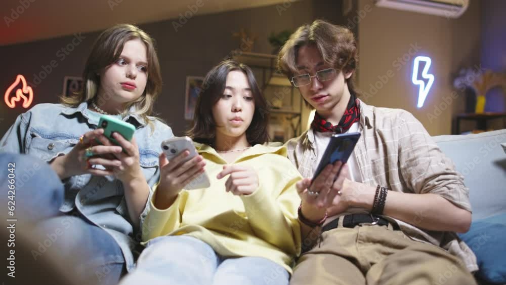 Three happy friends stick to their phones at home. They show jokes to ...