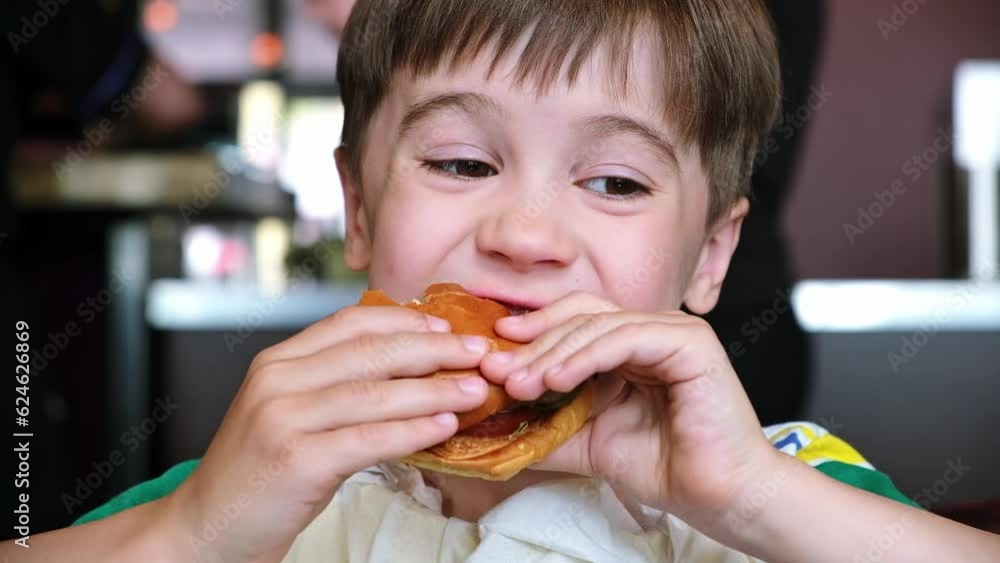 Cute little kid eating hamburger. Little boy in fast food cafe eats ...