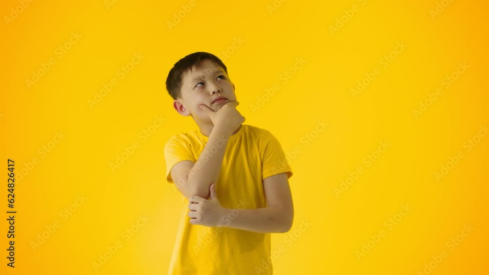 Asian kid boy wondering and thinking stroking his chin with a hand on a ...