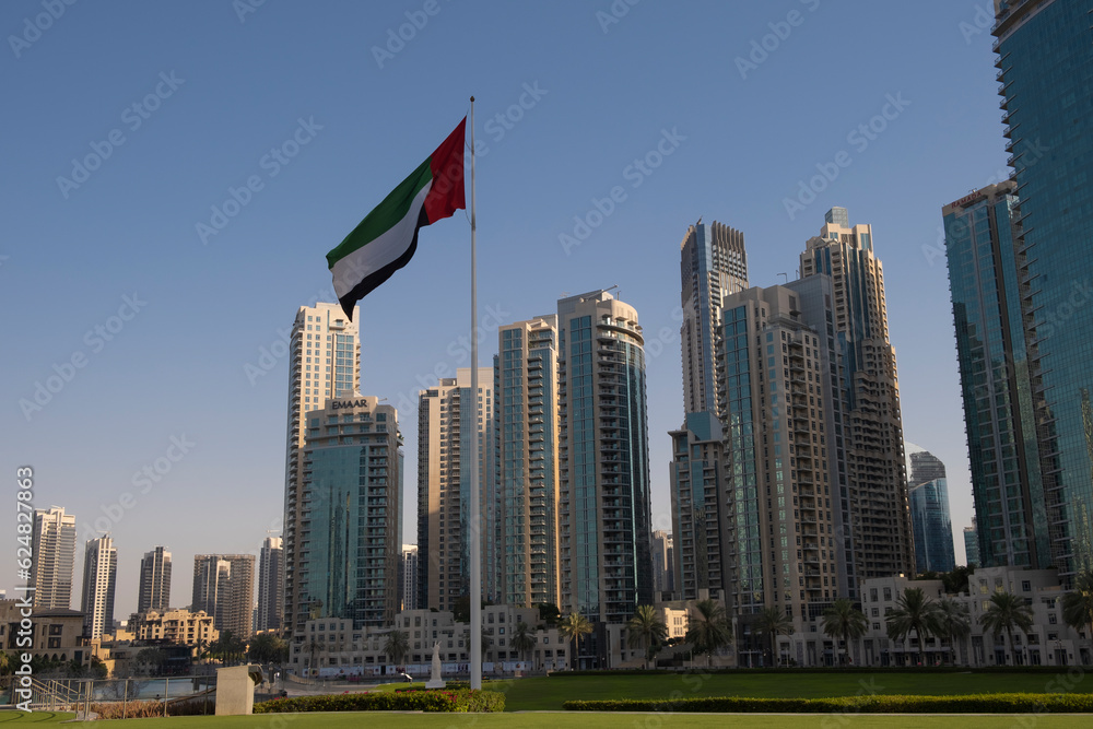 UAE flag waving on a mast against blue sky with highrise skyscraper ...