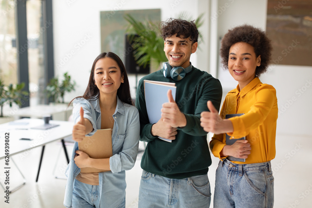 Happy diverse students gesturing thumbs up, standing in coworking space ...