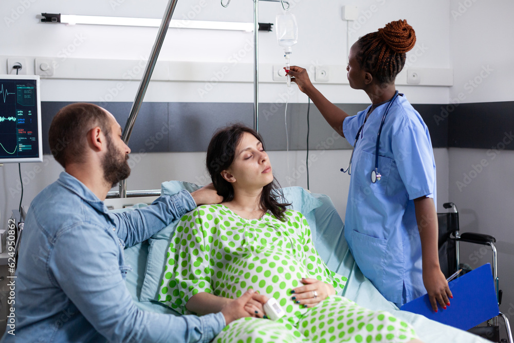 African american nurse checking pregnant woman iv drip, preparing for ...