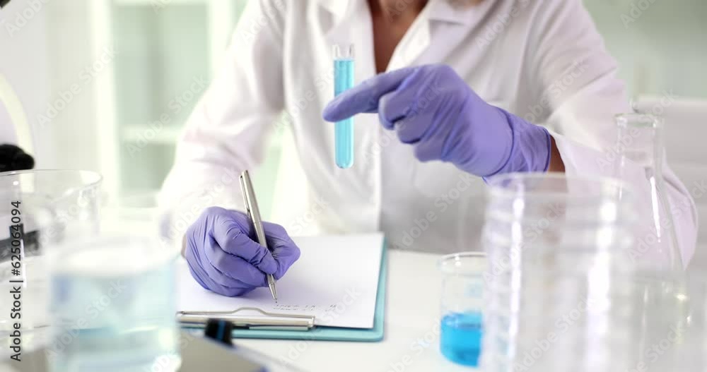 Scientist holds test-tube with examined blue reagent writing down ...