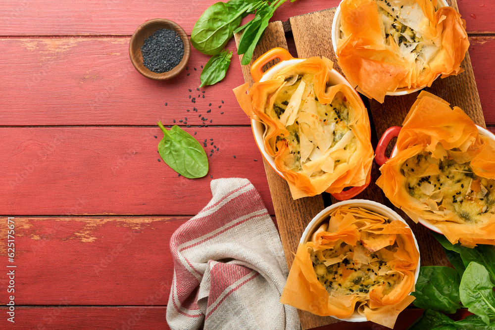 Filo pies with soft feta cheese and spinach in ceramic molds on old red ...