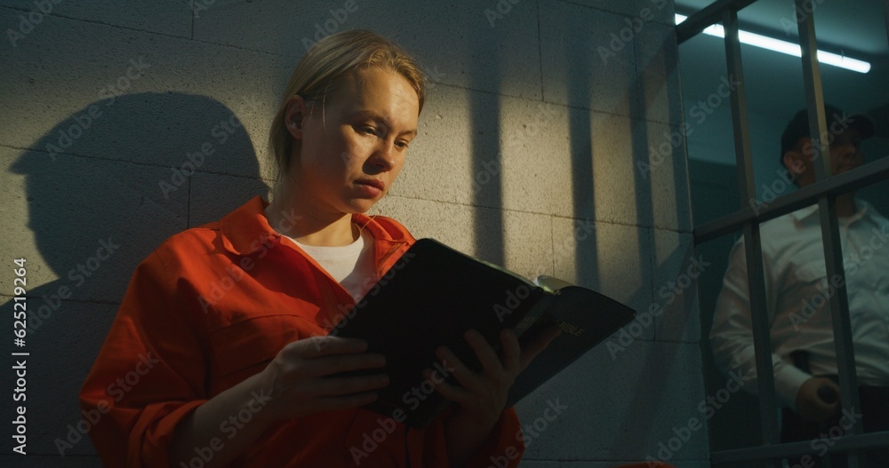 Female prisoner in orange uniform sits on bed in prison cell, reads ...