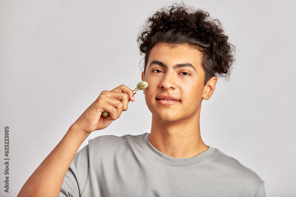 Young handsome smiling guy using jade de-puffing face roller to keep ...