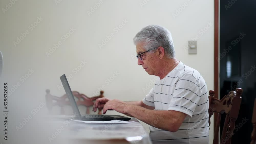 Candid senior man typing on laptop keyboard at home. Authentic domestic ...