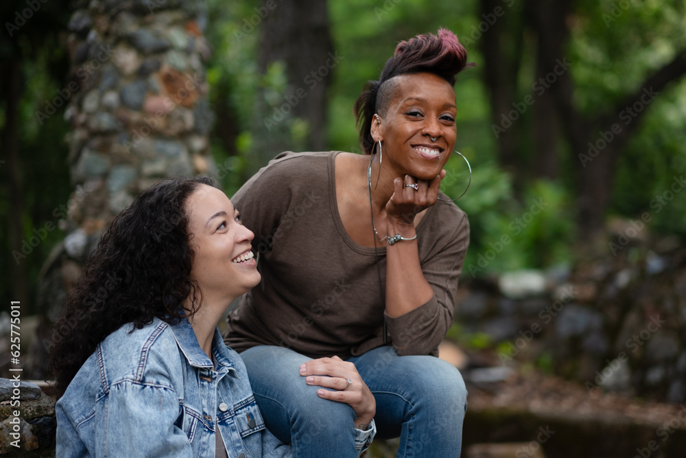 Two women poses for their engagement photos together. They are seated ...