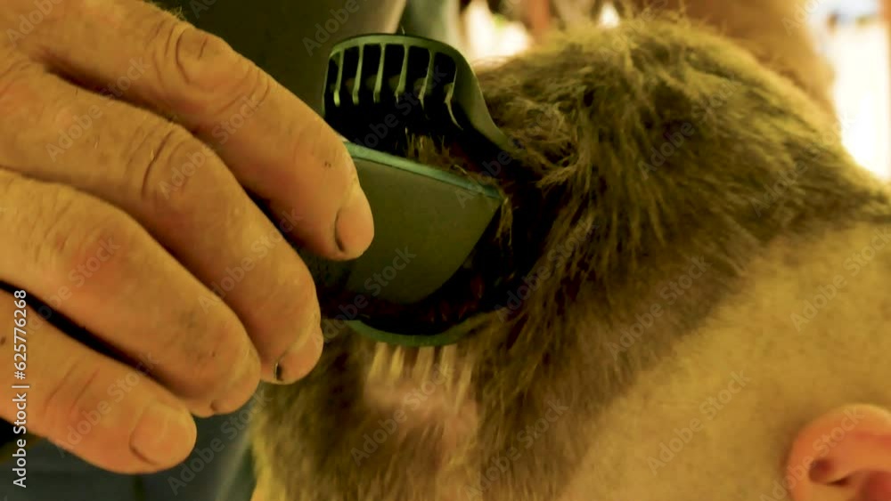 A man's hand runs an electric hair clipper over the boy's head, cuts ...