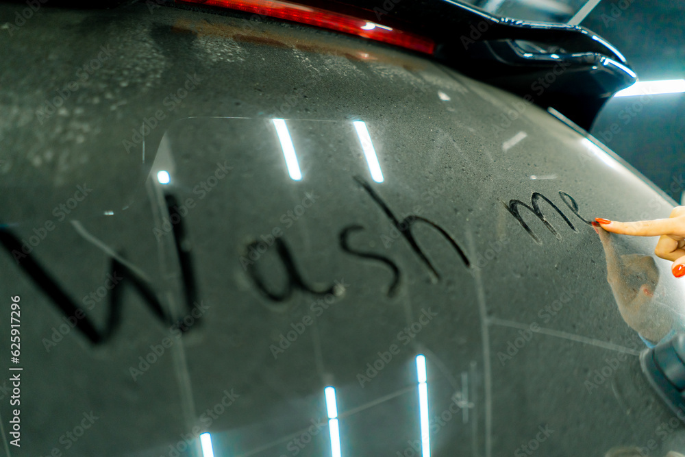 A close-up of a woman's hand with a red manicure writing "wash me" on ...
