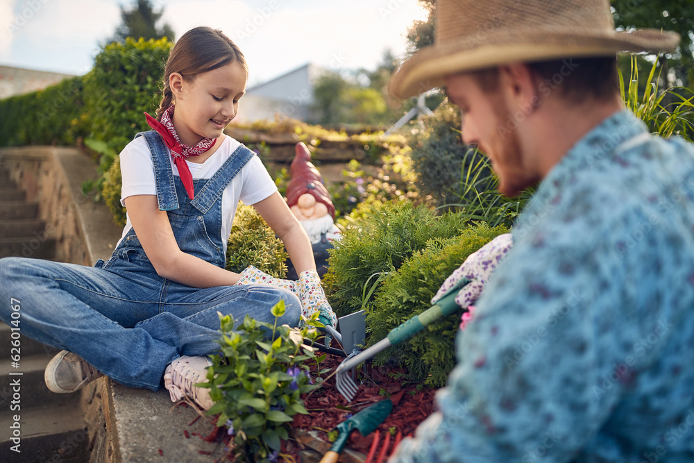 Beautiful young girl using garden rake sitting by the garden outdoors ...