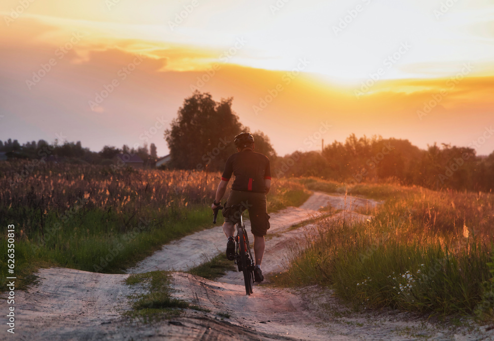 Cyclist riding a trail in a field on a gravel bike on a dramatic sunset ...