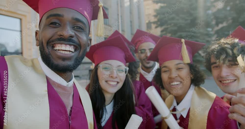 Portrait of men and women in graduation hats and gowns making online ...
