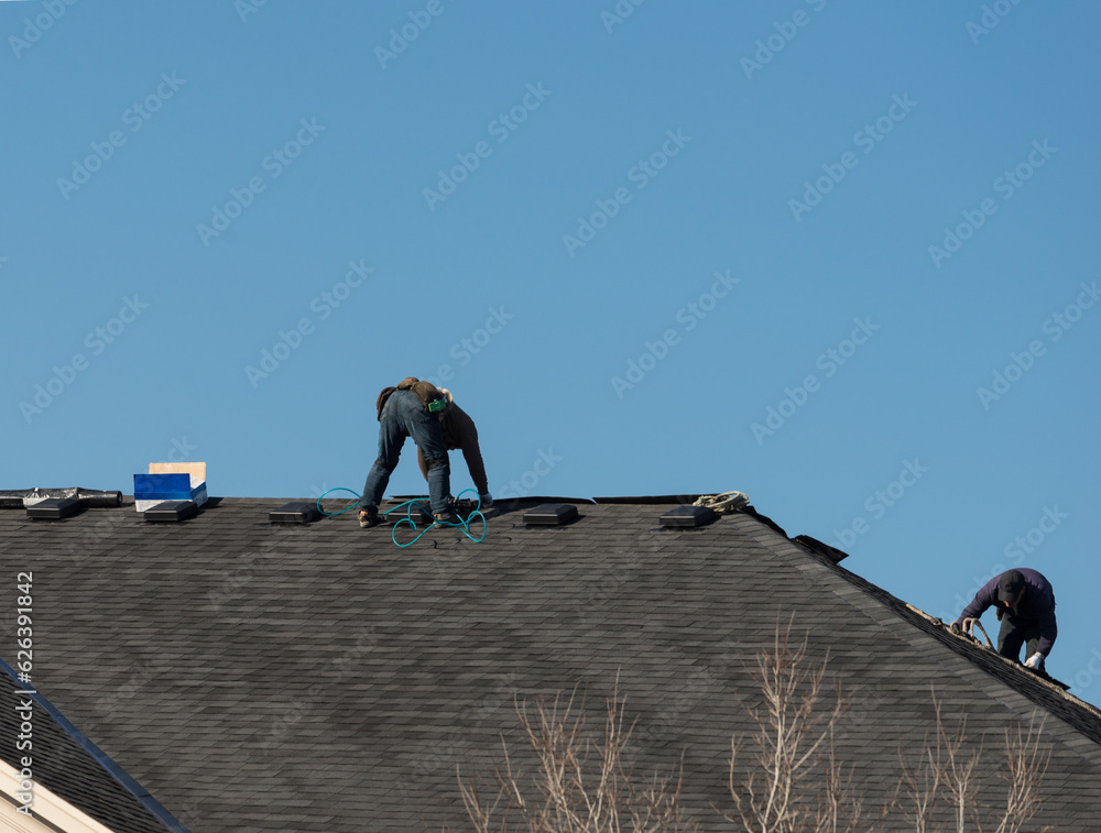 Two roofing workers on the roof replacing asphalt shingles Stock Photo ...