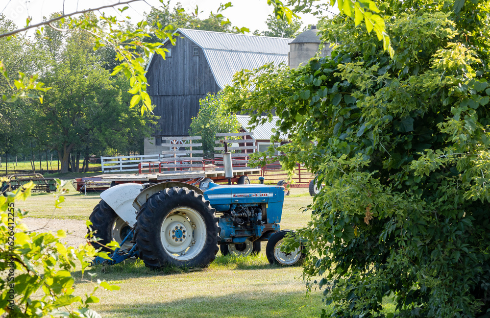 A Ford 4000 tractor in front of a barn framed by trees with hay wagons ...