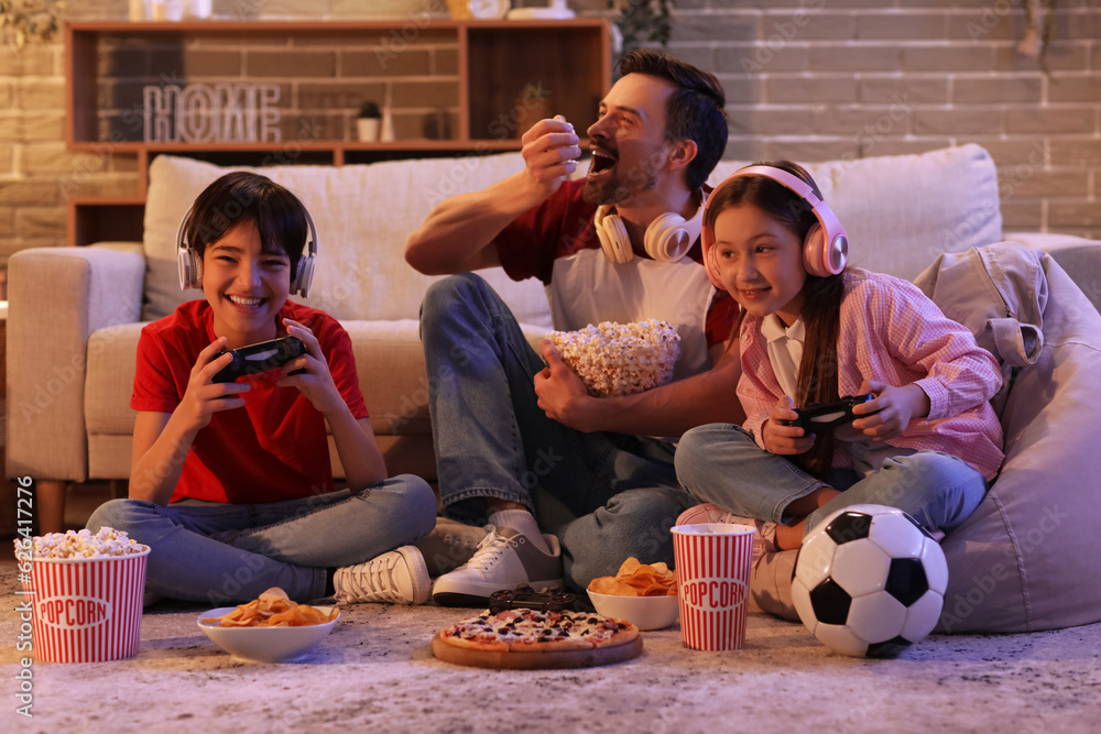 Father eating popcorn while his little children playing video game at ...