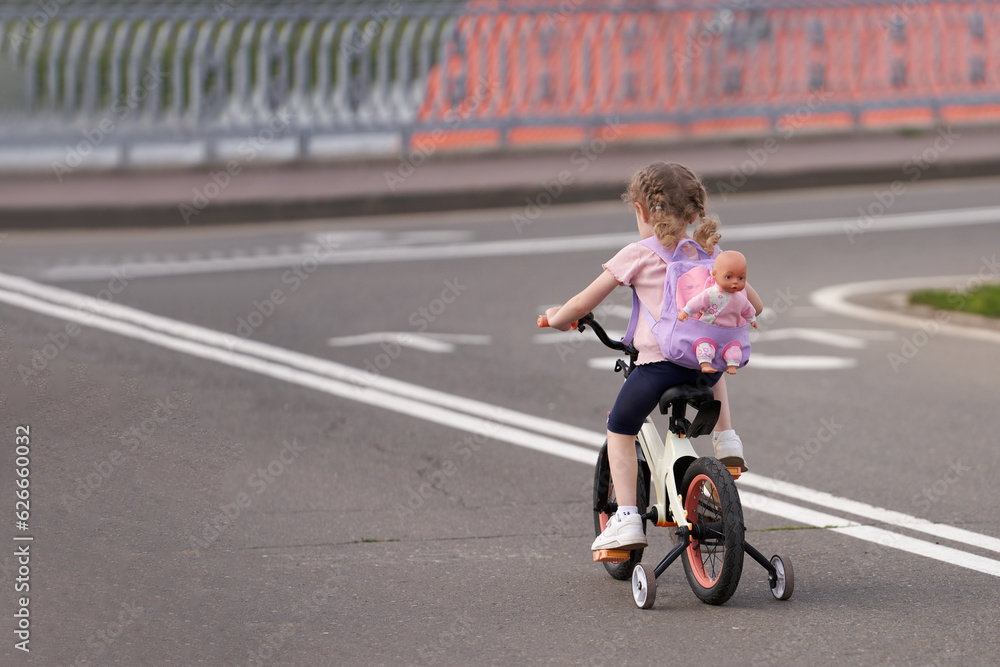 A little blonde girl rides a two-wheeled children's bicycle with ...