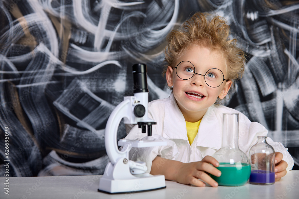 An enthusiastic Caucasian child is sitting at a table with test tubes ...