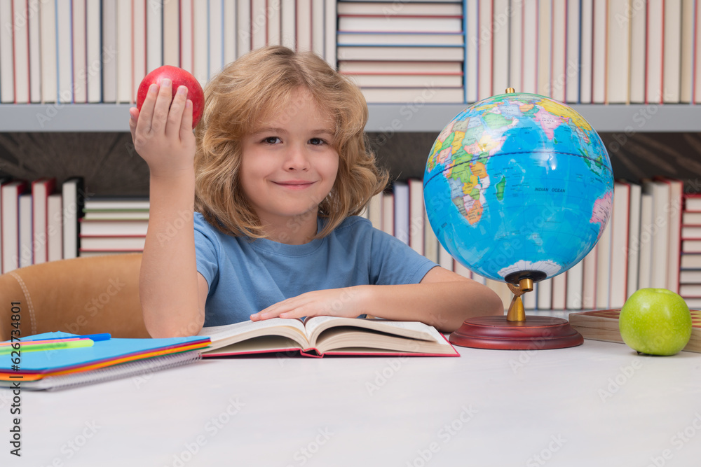 School boy with books and apple in library. School kid looking at globe ...